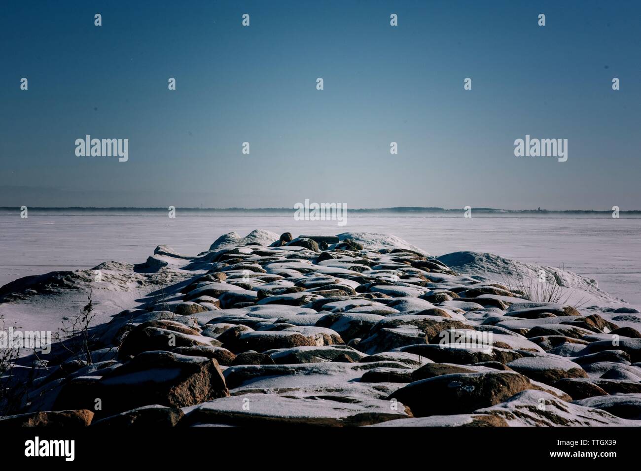 snow covered rocks leading to frozen lake in Canada with blue skies ...