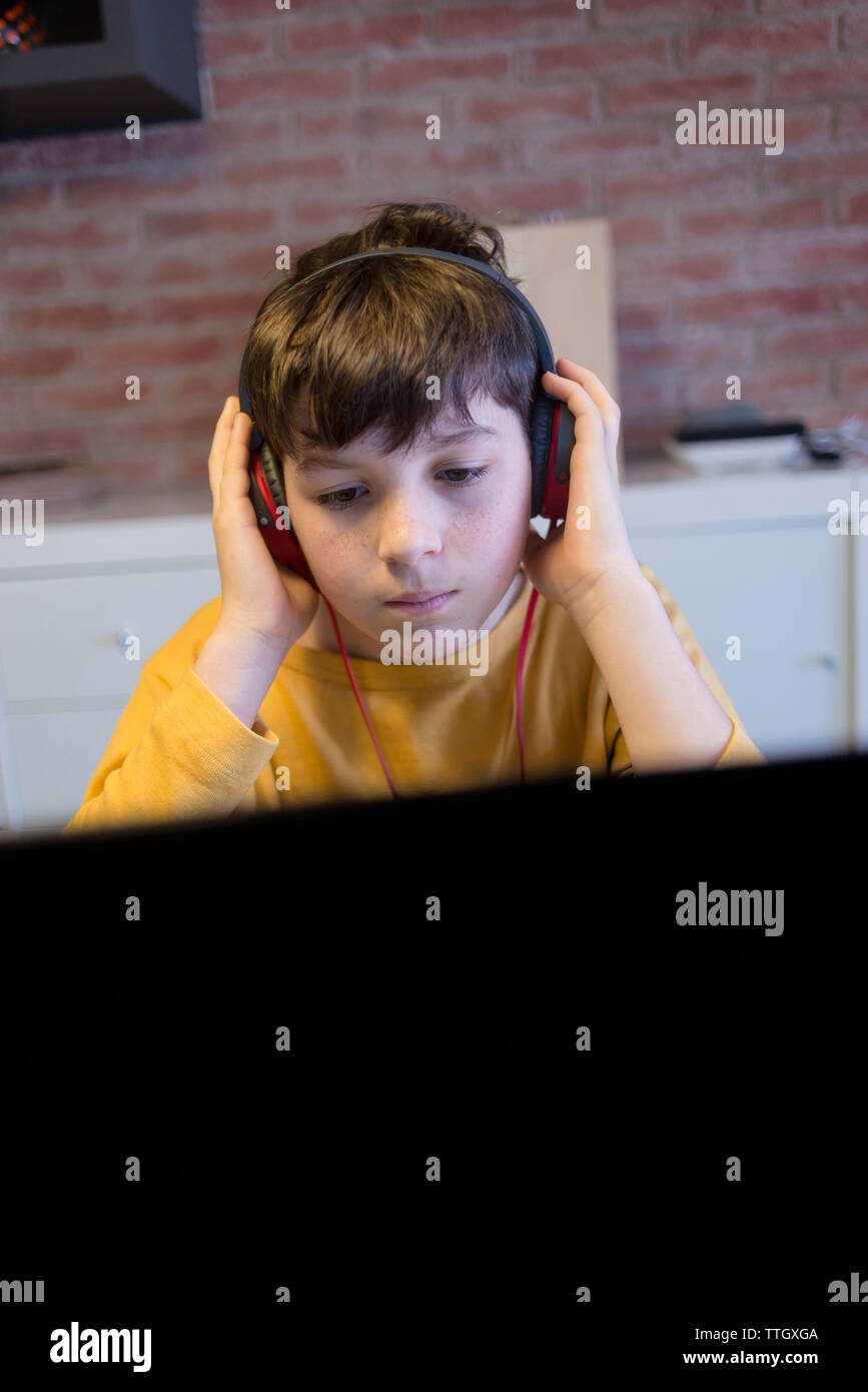 Boy using headphones and laptop computer while studying at home Stock ...