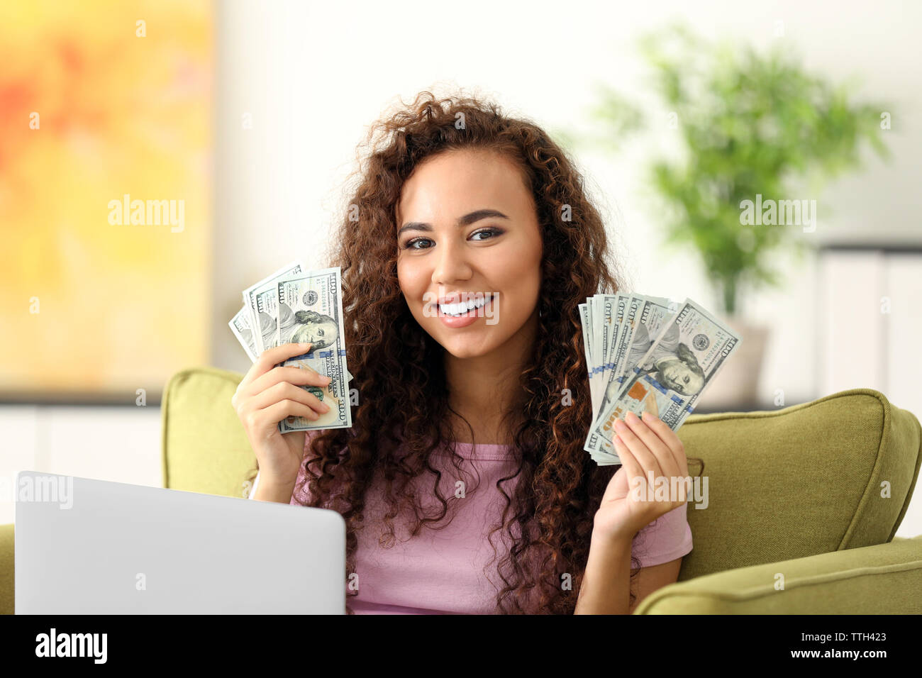 Beautiful young girl with cash and laptop on armchair Stock Photo - Alamy