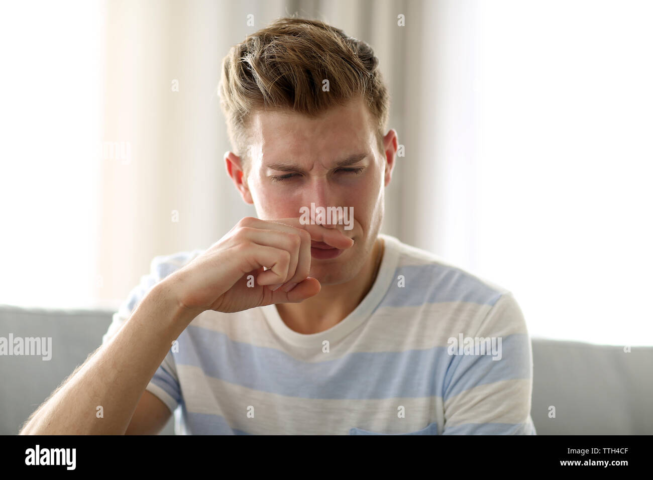 Young blonde man pinching his nose because of the stench in the room ...