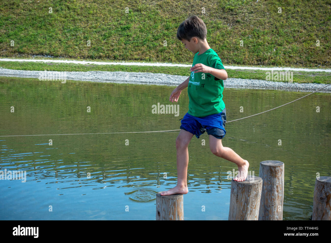 Young boy balancing on a rope above a pond at a water playground Stock ...