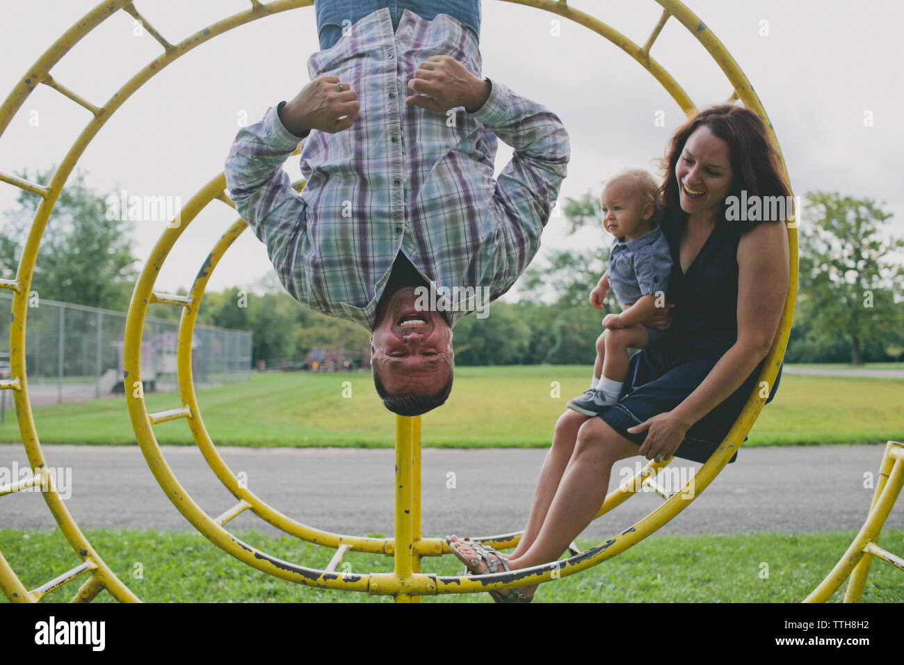 Mother and son looking at father hanging on circular monkey bars in ...