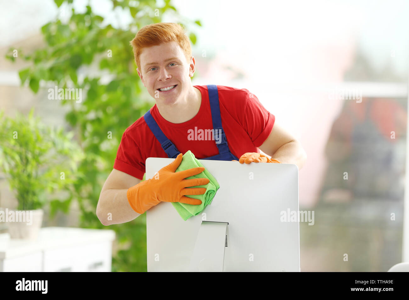 Young janitor cleaning computer monitor in office Stock Photo - Alamy