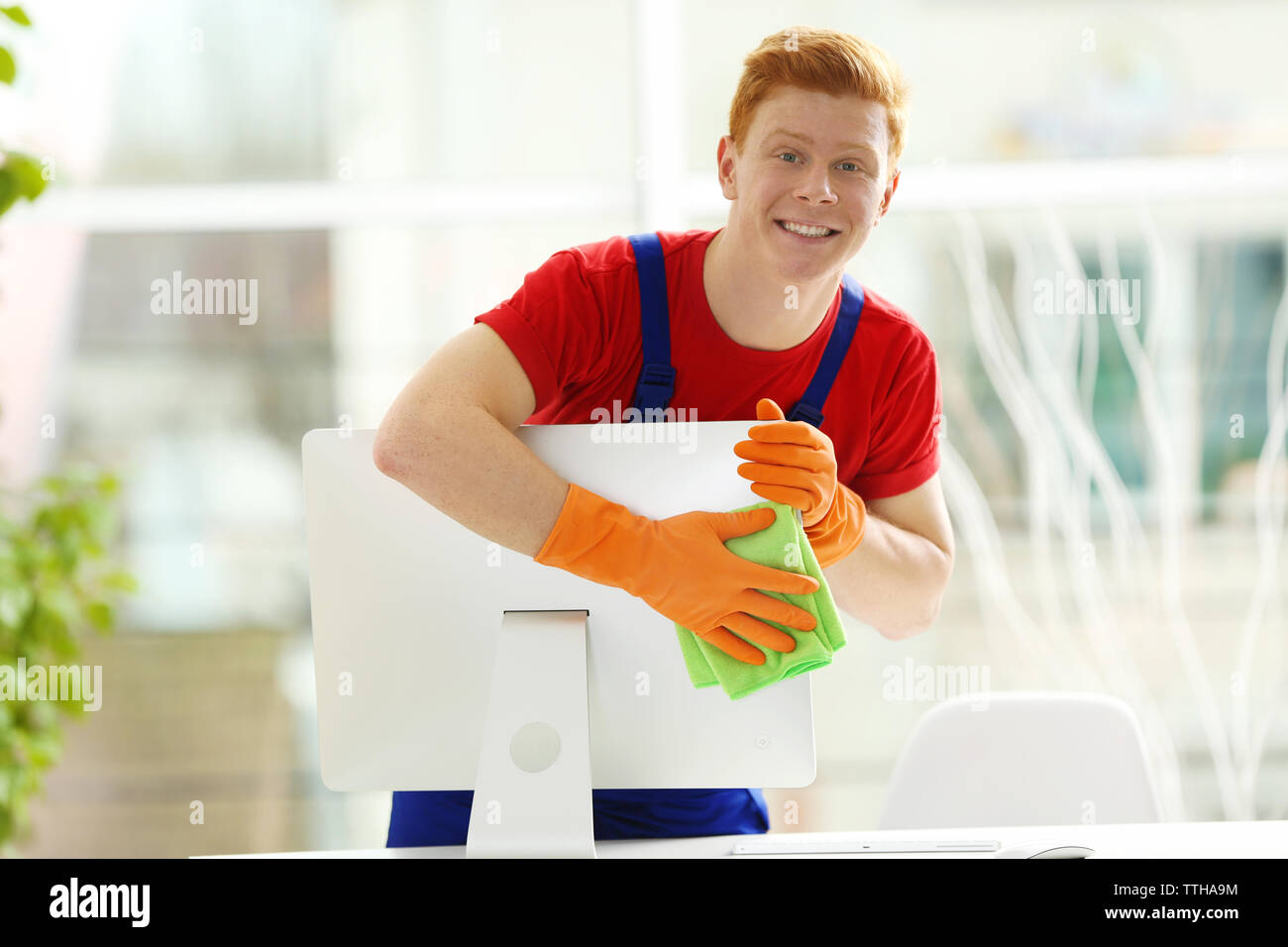 Young janitor cleaning computer monitor in office Stock Photo - Alamy