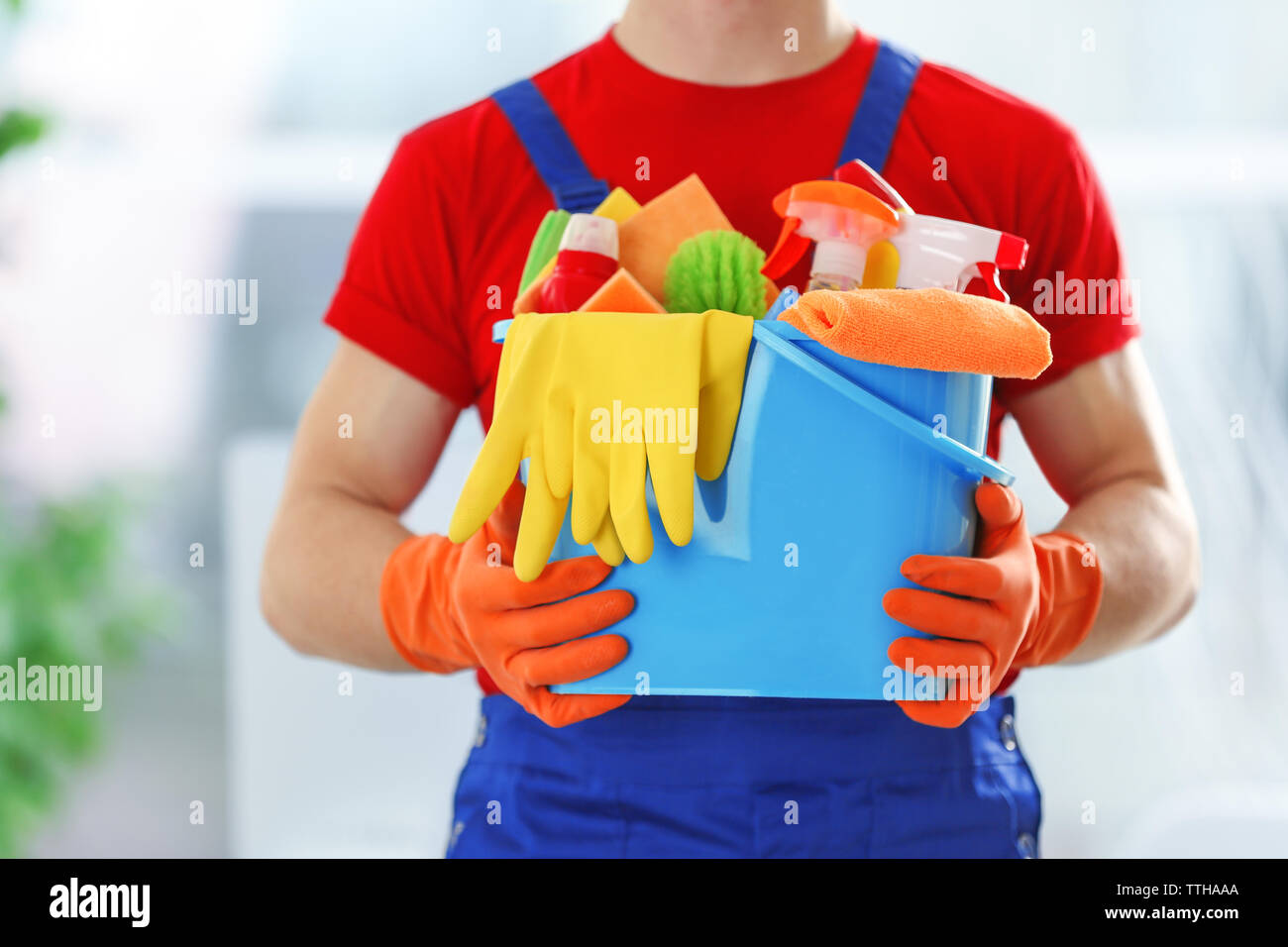 Young janitor holding cleaning products and tools on bucket, close up ...