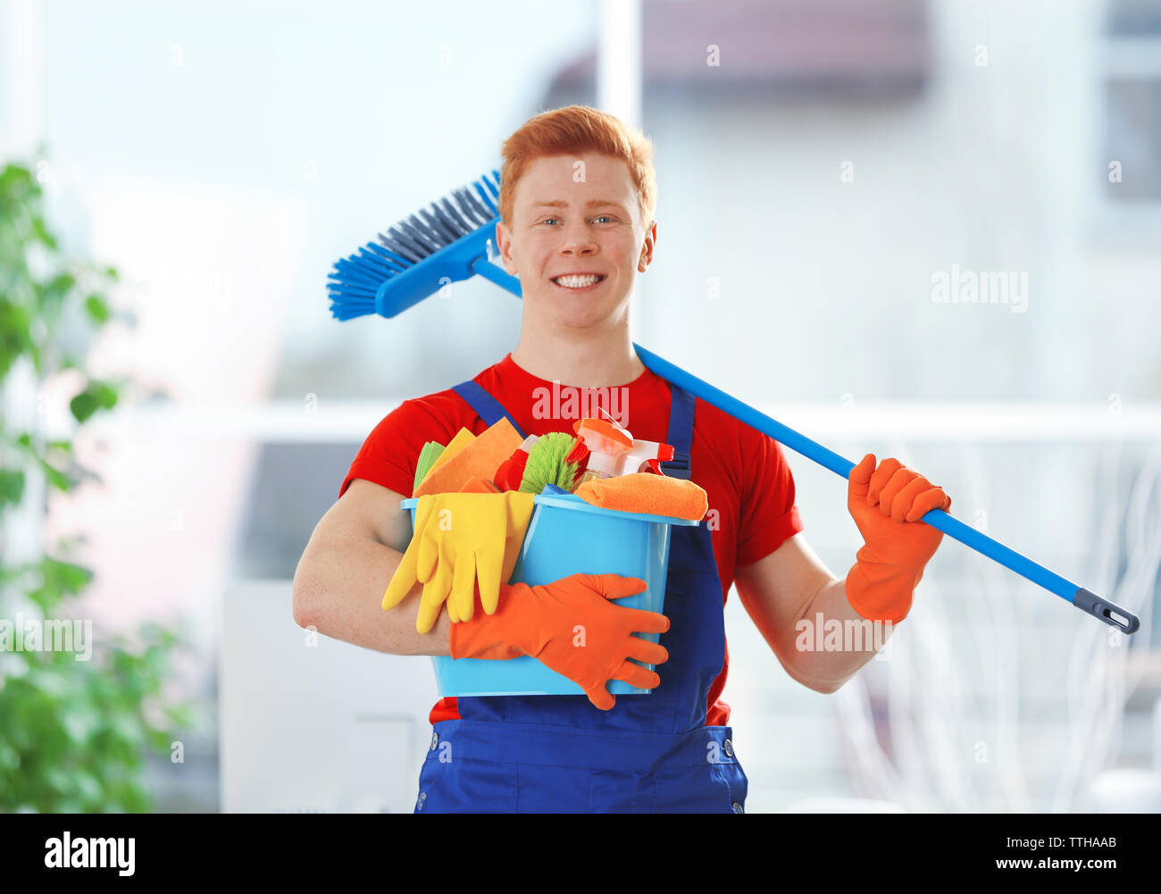 Young janitor holding cleaning products and tools in office Stock Photo ...
