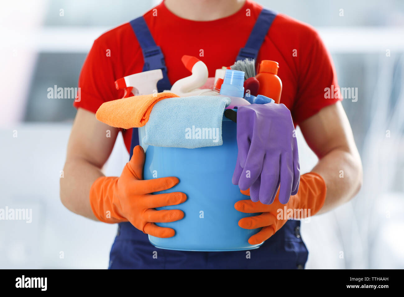 Young janitor holding cleaning products and tools on bucket, close up ...