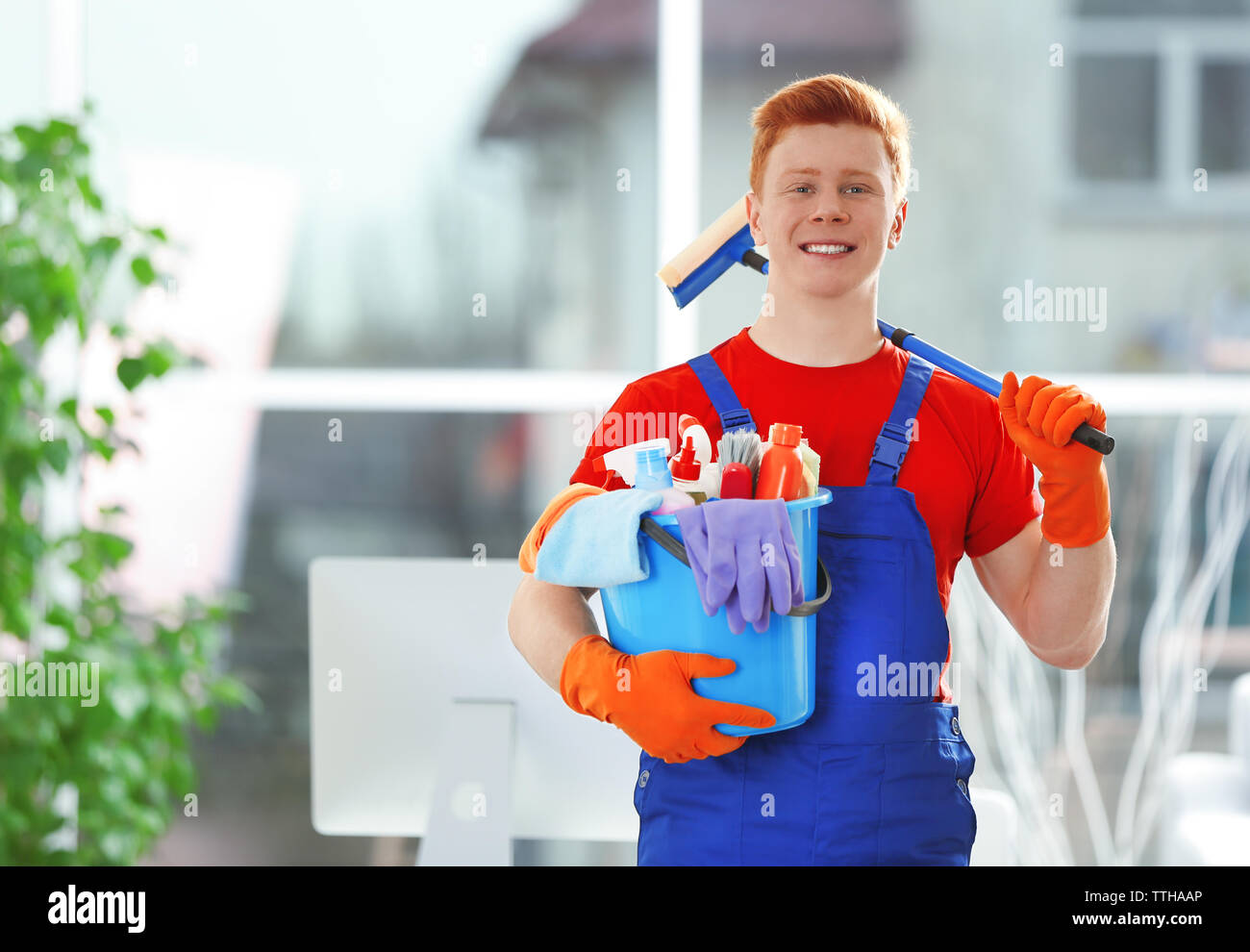 Young janitor holding cleaning products and tools in office Stock Photo ...