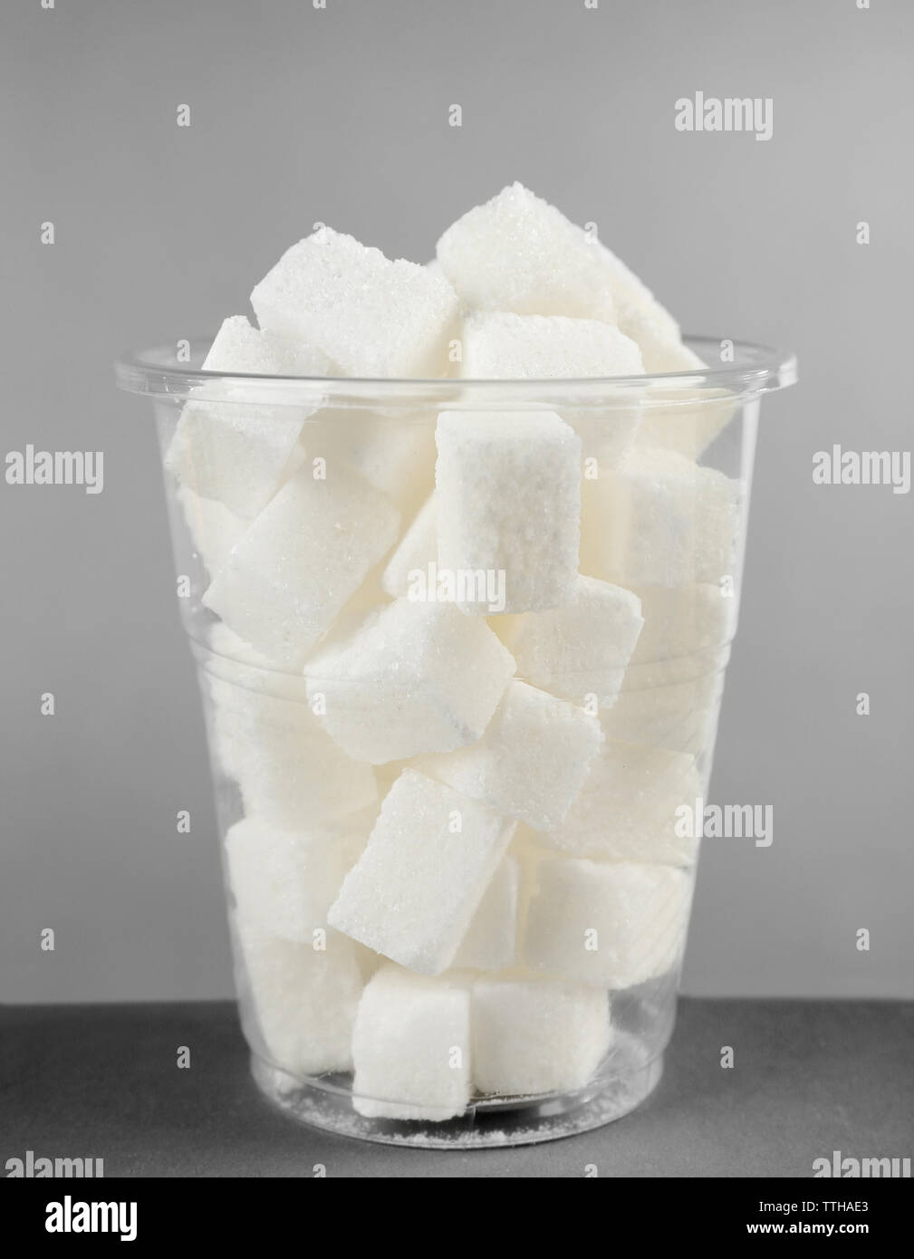 Plastic glass full of sugar on grey background Stock Photo - Alamy