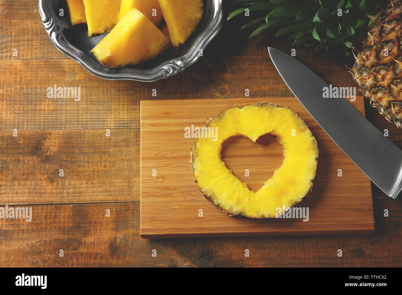 Juicy pineapple slice with cut out heart shape on wooden cutting board ...