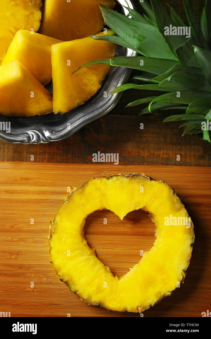 Juicy pineapple slice with cut out heart shape on wooden cutting board ...