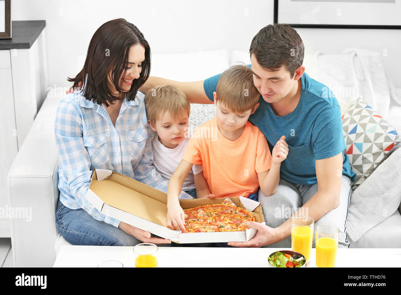 Happy family eating pizza on sofa all together Stock Photo - Alamy