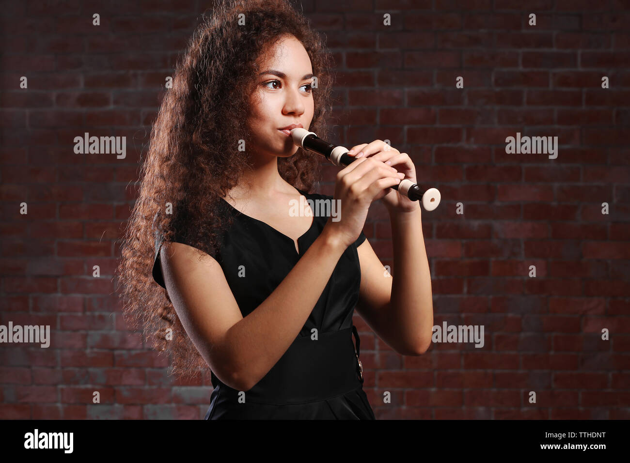 Beautiful young woman playing on recorder over brick wall background ...