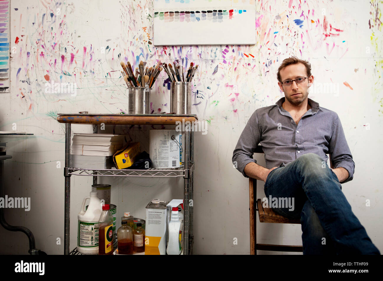 Portrait of male artist sitting on chair against wall in workshop Stock ...