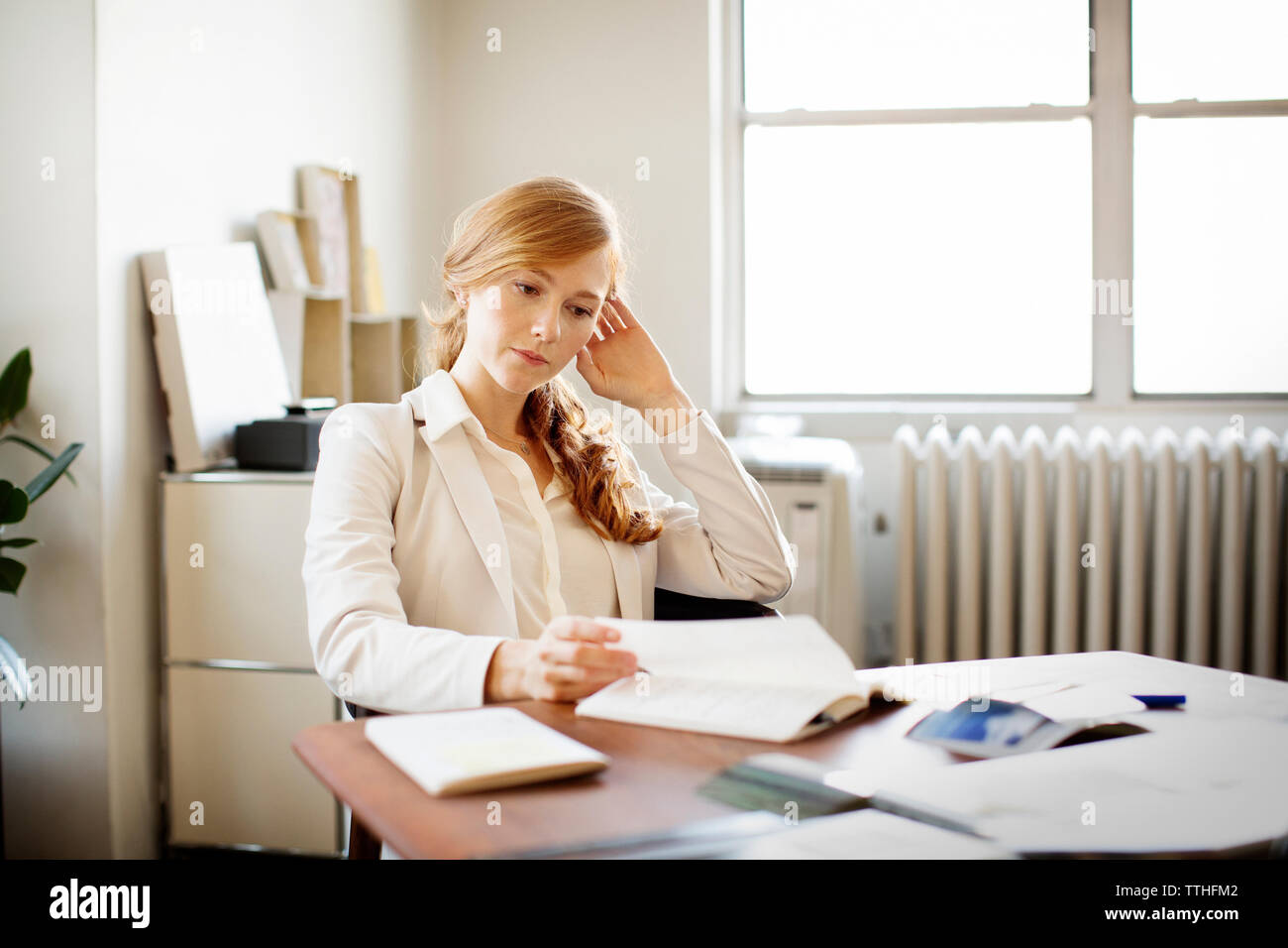 Female reading book while sitting at desk in office Stock Photo - Alamy