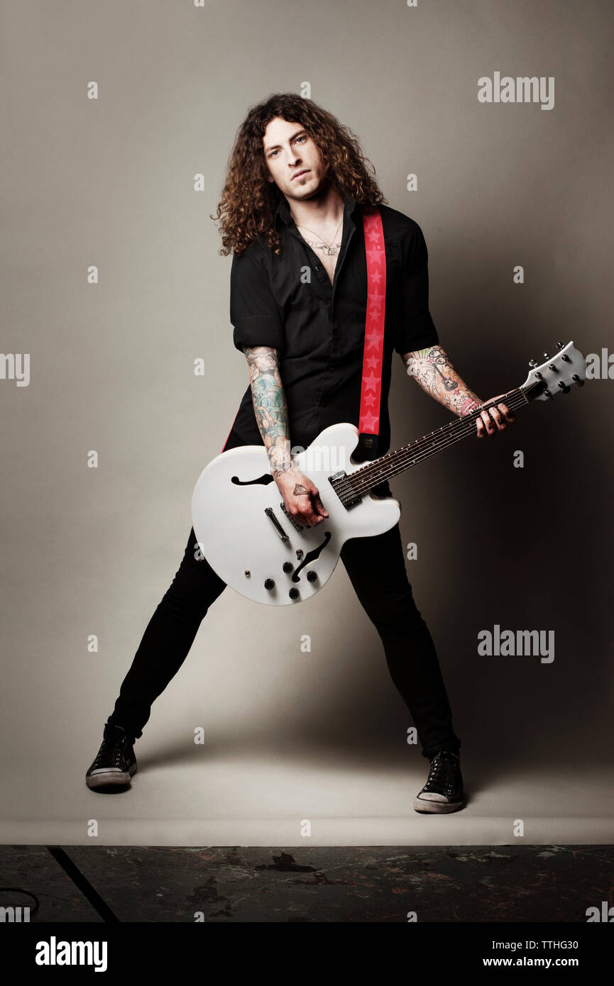 Full length portrait of guitarist standing against wall Stock Photo - Alamy