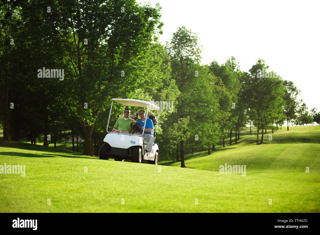 Male golfers driving golf cart on field Stock Photo - Alamy