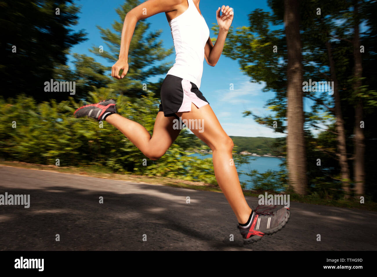Low section of jogger running on road against trees Stock Photo - Alamy