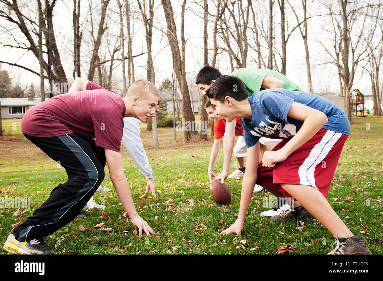 Smiling friends playing American football while bending over field in ...