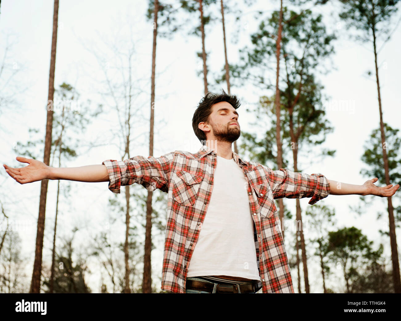 Man with arms outstretched standing against trees in forest Stock Photo ...