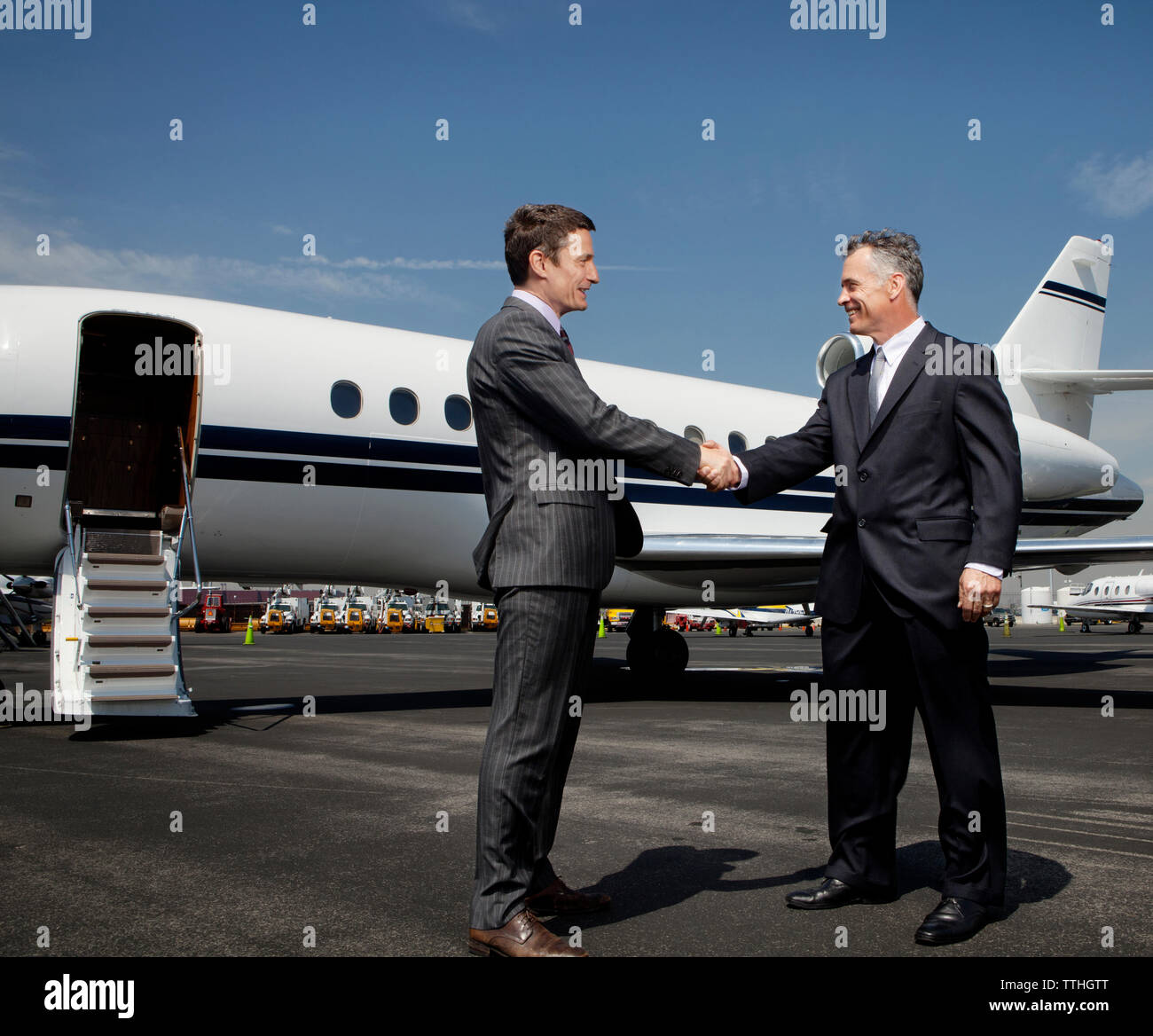 Happy businessmen doing handshake against corporate jet on runway Stock ...