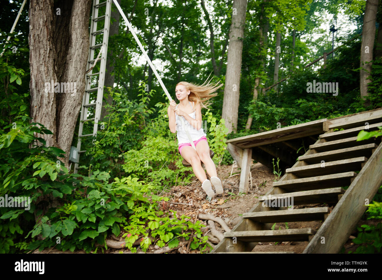 Young woman swinging on rope by staircase in forest Stock Photo - Alamy