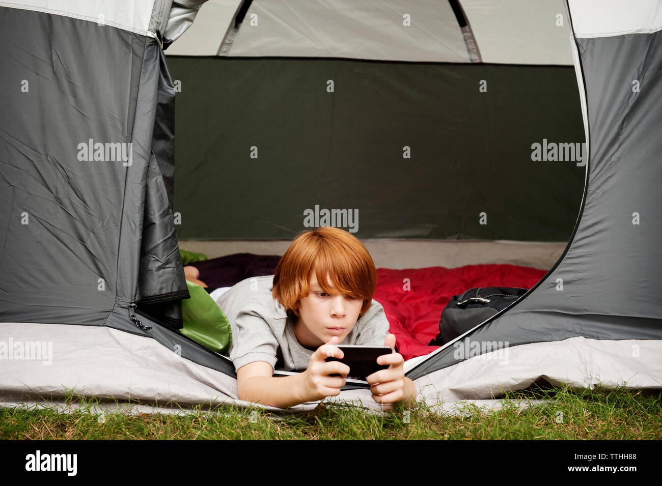 Boy using phone while lying on front in tent Stock Photo - Alamy