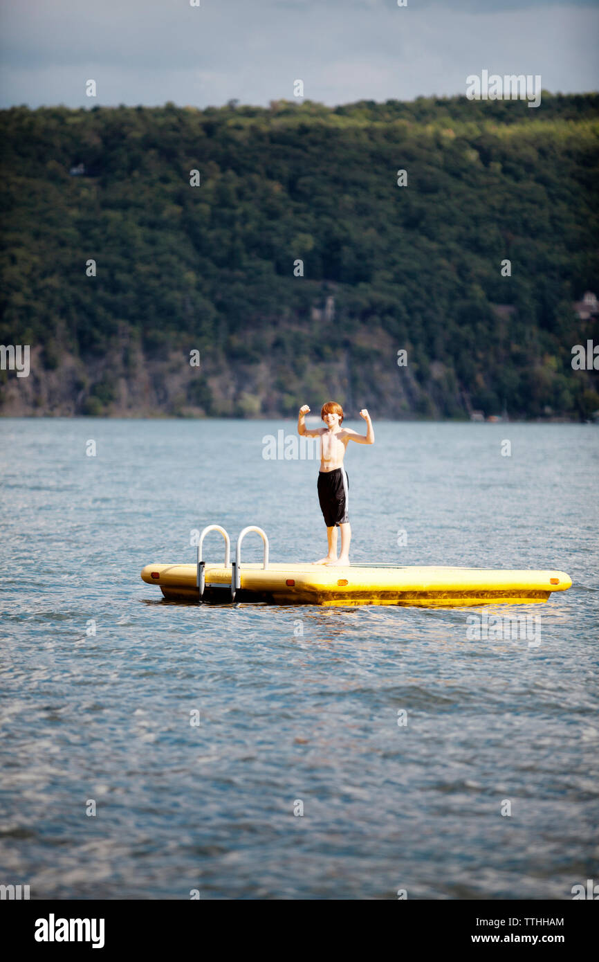 Boy flexing muscles while standing on floating platform in lake Stock ...