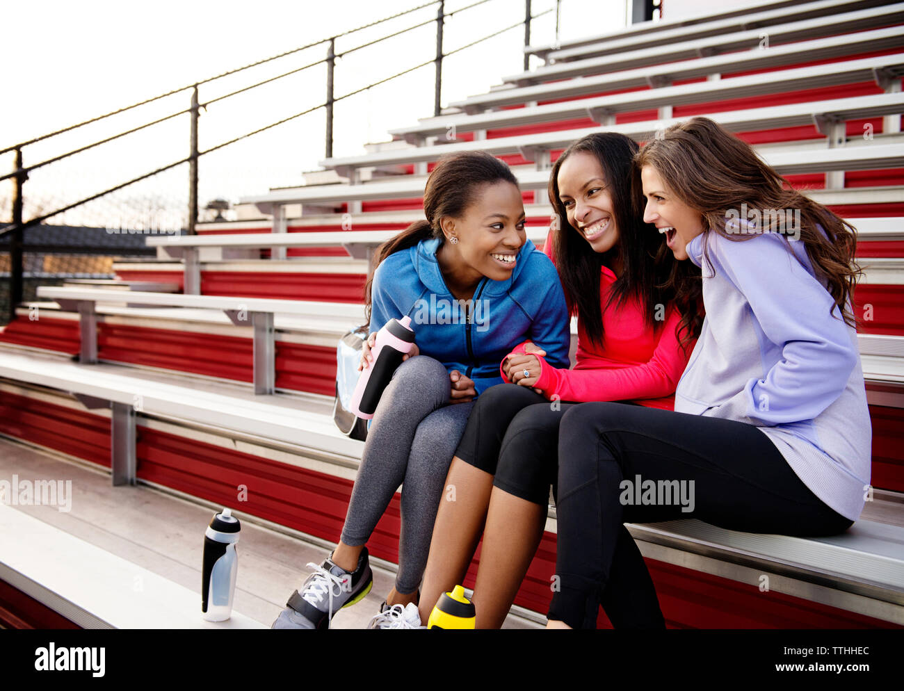 Happy friends talking while sitting on steps in stadium Stock Photo - Alamy