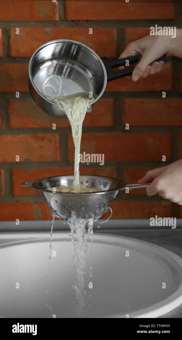 Female hands pouring water from boiled spaghetti over sink in the ...