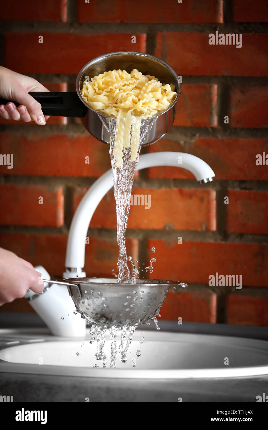 Female hands pouring water from boiled pasta over sink in the kitchen ...