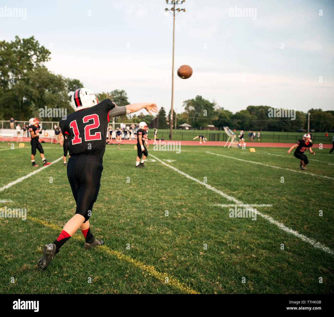 Rear view of teenage American football player throwing ball at field ...
