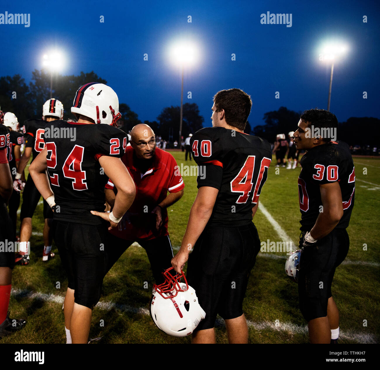Rear view of American football players listening to coach on ...