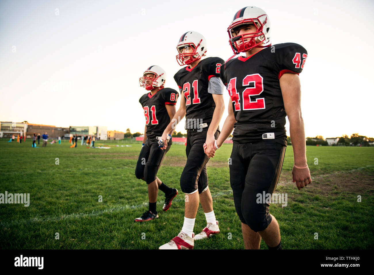 American football players holding hands and walking on grassy field ...