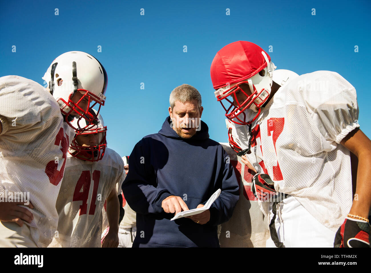 Coach sharing strategy to American football players standing on field ...
