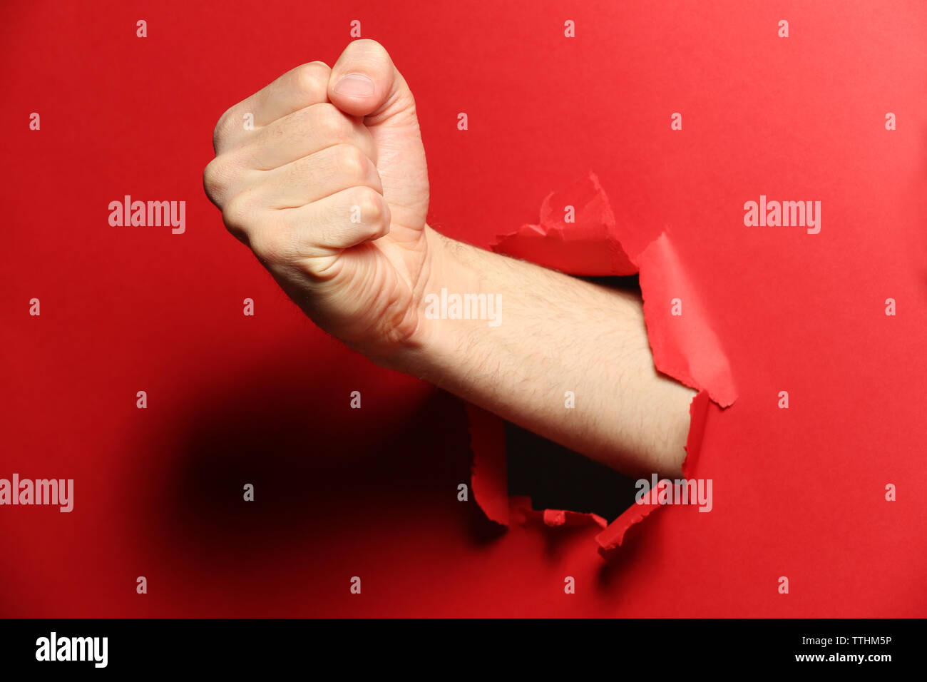 Male fist punching through red paper Stock Photo - Alamy