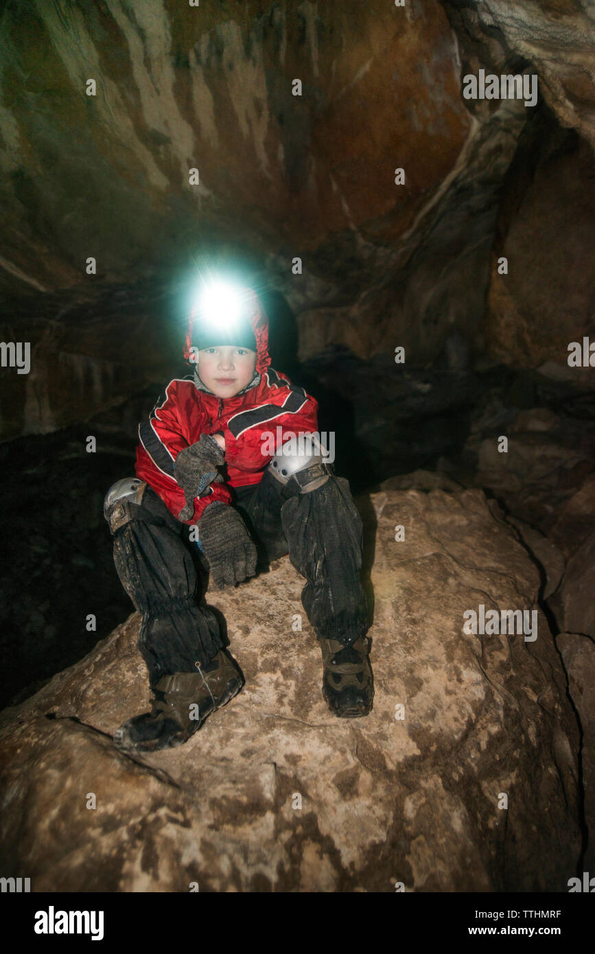 Portrait of boy wearing illuminated headlamp while sitting on rock in ...