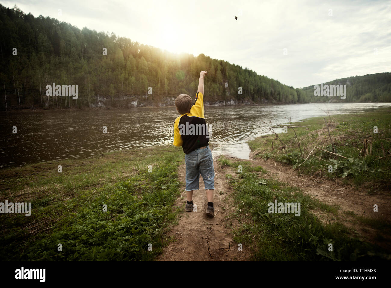 Rear view of boy throwing stone at river Stock Photo - Alamy
