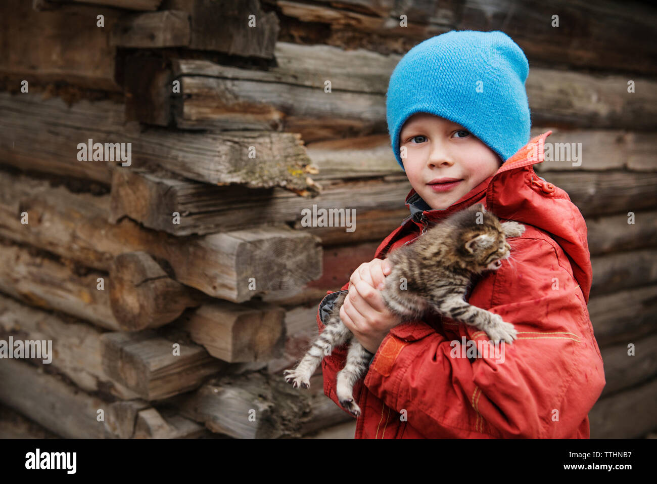 Portrait of boy carrying cat while standing against wooden wall Stock ...