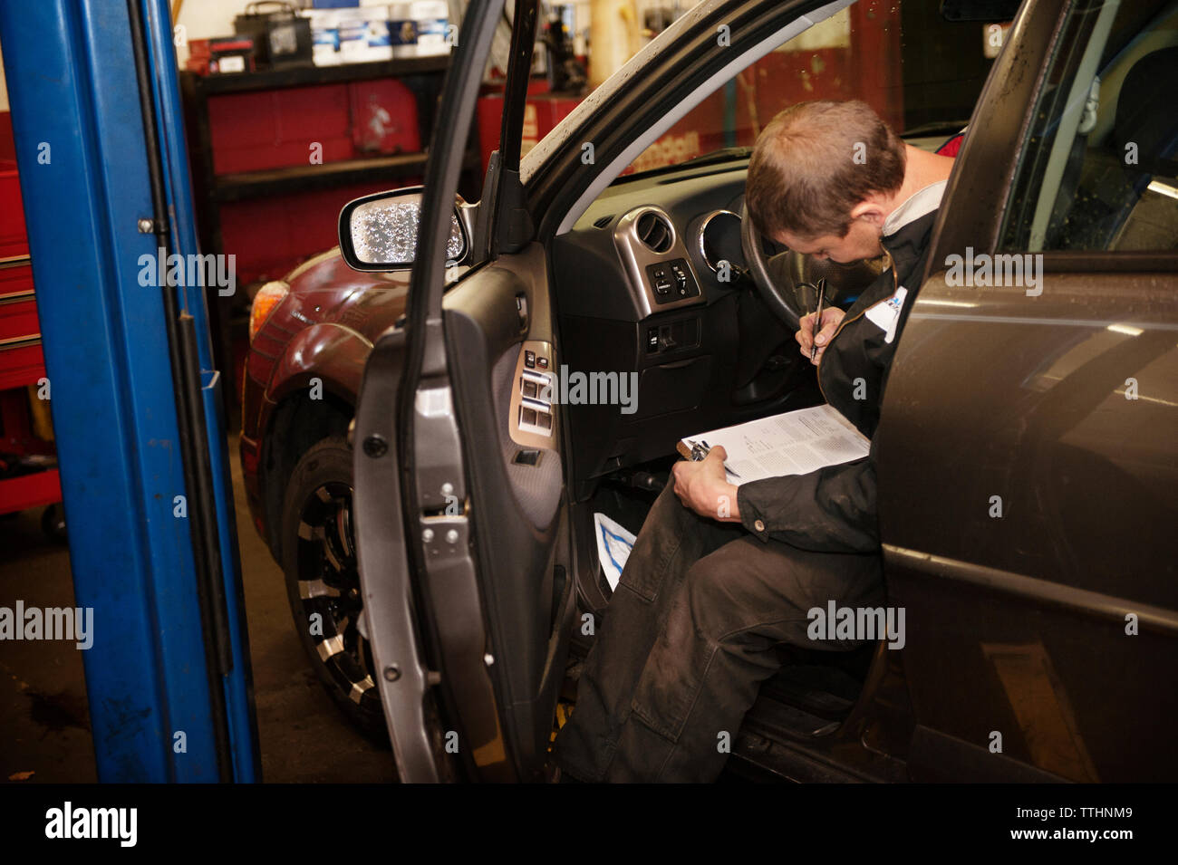 Mechanic writing while sitting in car at garage Stock Photo - Alamy