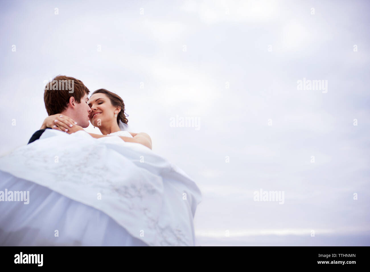 Groom carrying bride against sky Stock Photo - Alamy