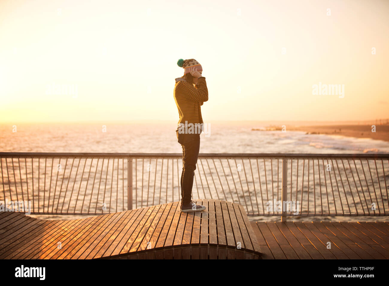 Side view of woman standing on boardwalk by beach during sunset Stock ...