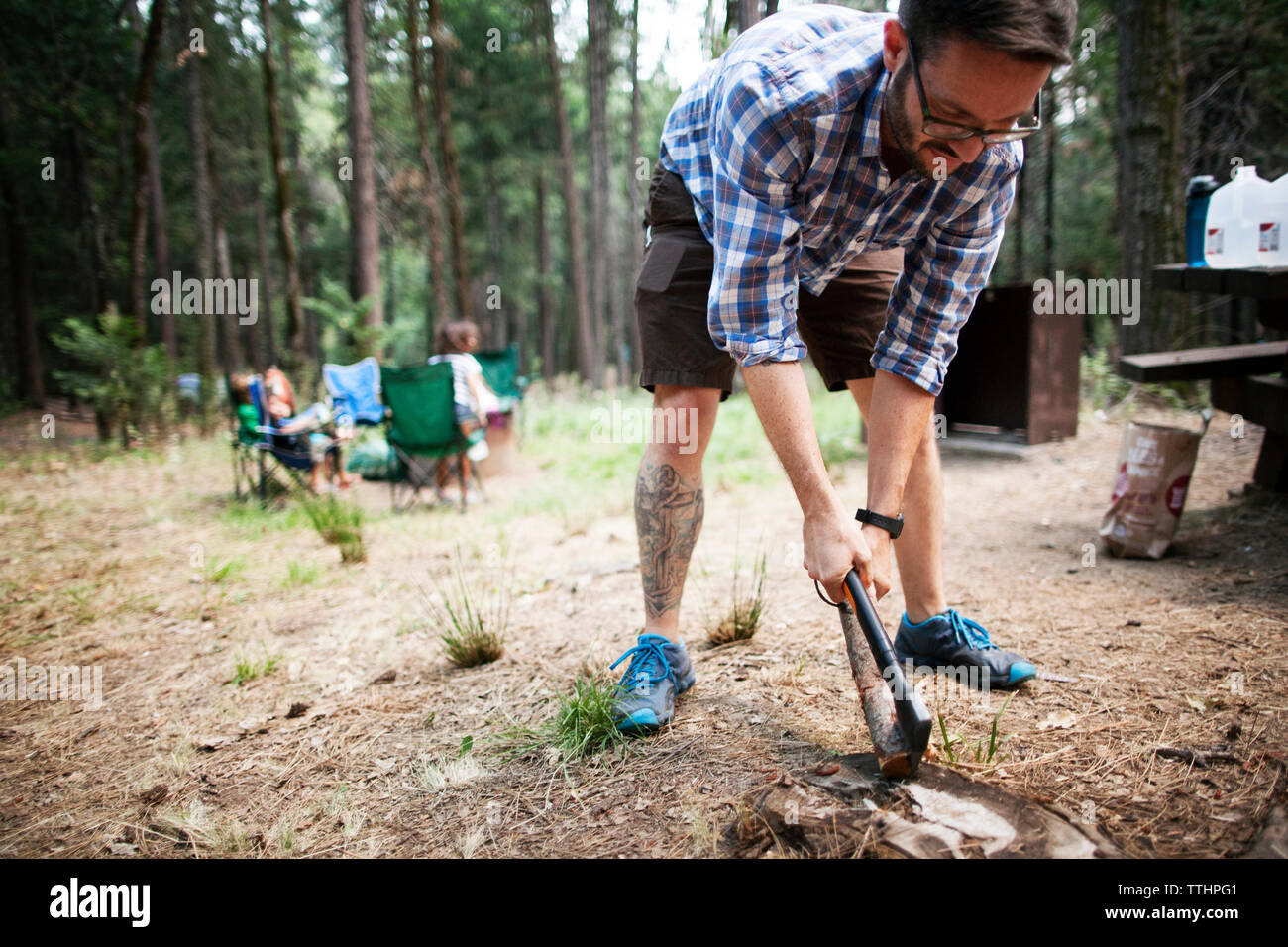 Father cutting wood with children in background at forest Stock Photo ...