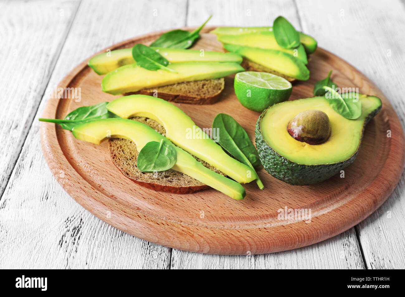 Slices of fresh avocado with bread on wooden cutting board closeup ...