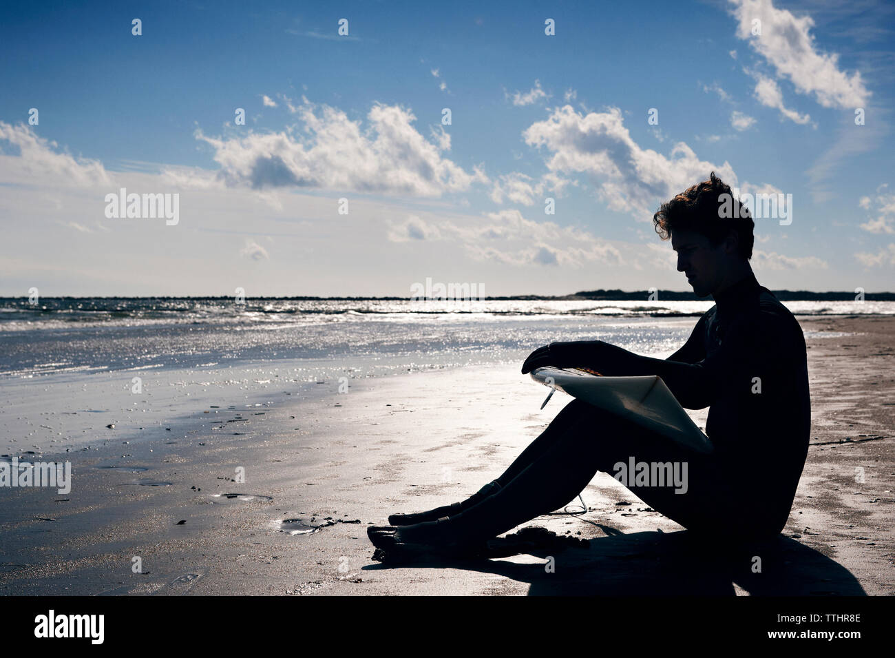 Side view of surfer with surfboard sitting on shore at beach during ...