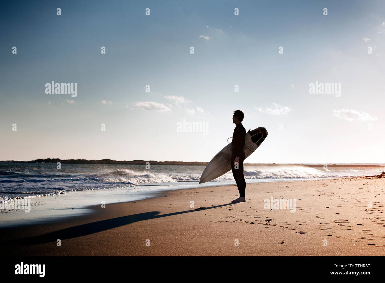 Side view of surfer carrying surfboard while standing on shore at beach ...