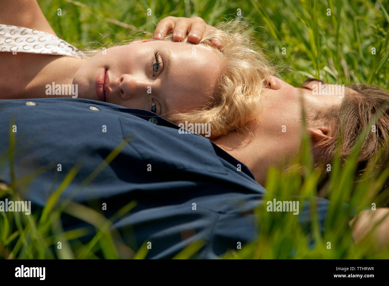 Portrait of woman leaning on man's chest while lying in grass field ...