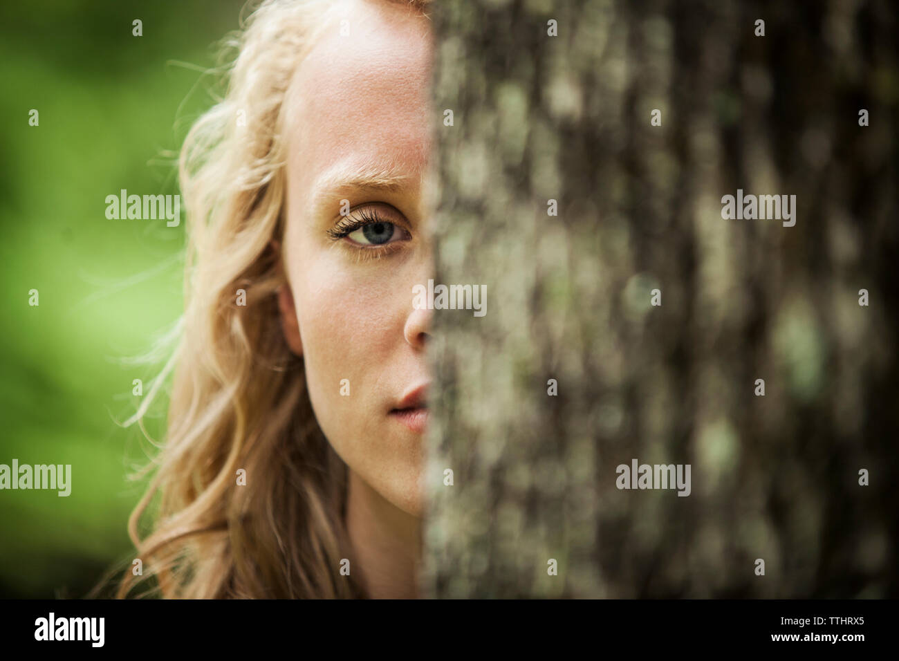 Portrait of woman standing behind tree Stock Photo - Alamy