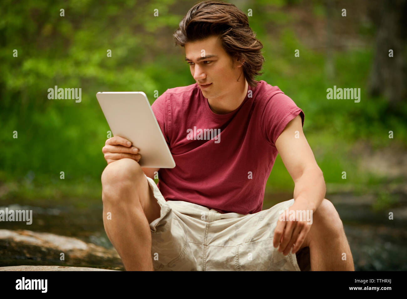 Young man using tablet computer while sitting on rocks Stock Photo - Alamy