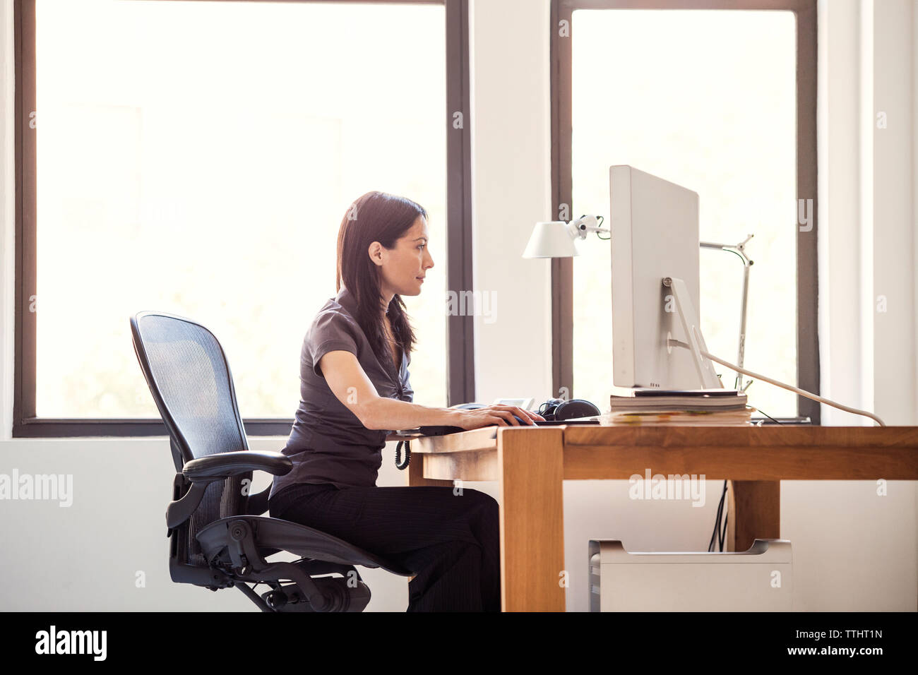 Side view of woman working on computer at office Stock Photo - Alamy